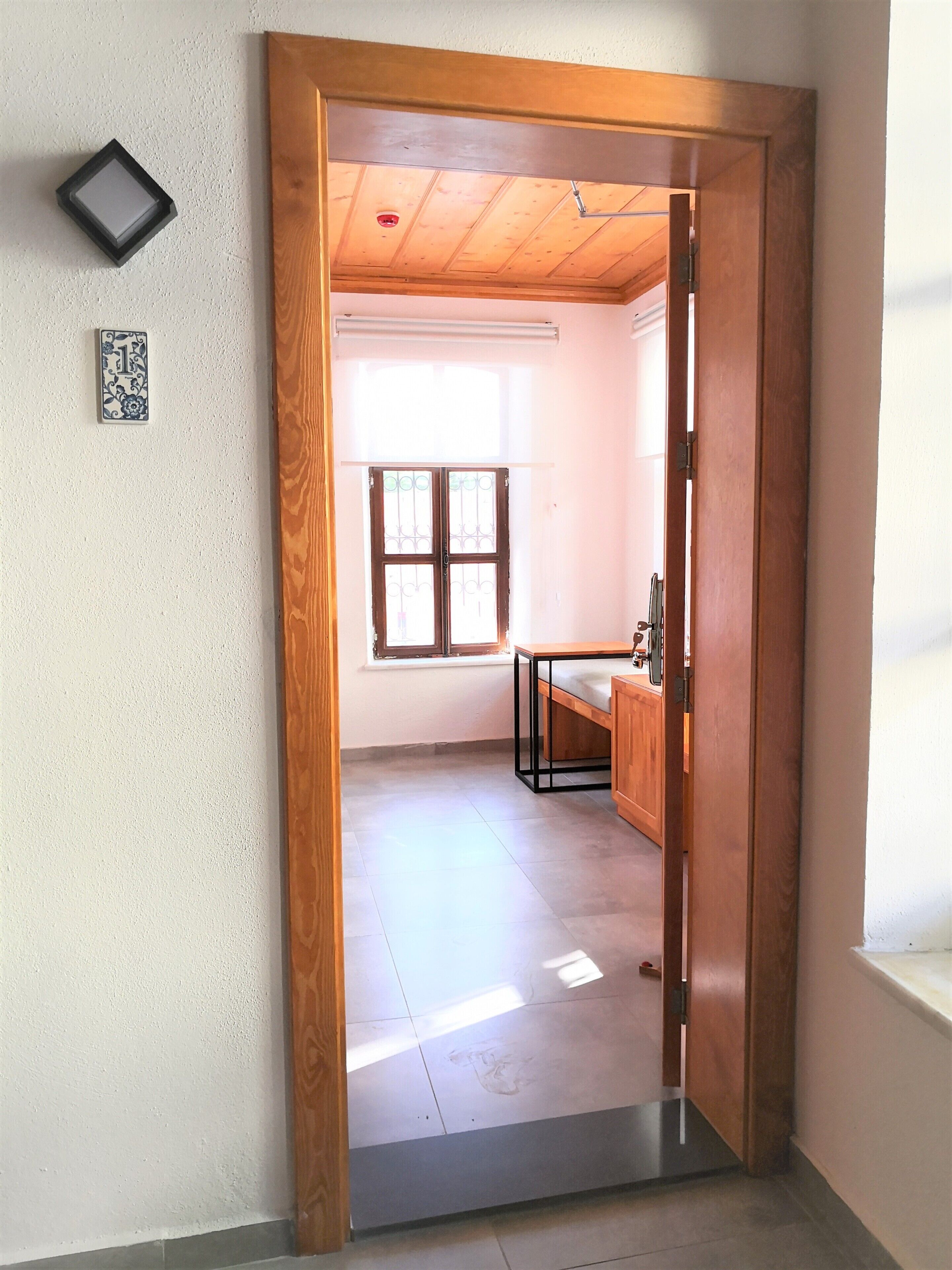 Quarto com porta de madeira, janela com grades, cama e uma pequena mesa.