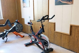 Duas bicicletas ergométricas em um espaço com lambris e um quadro na parede.