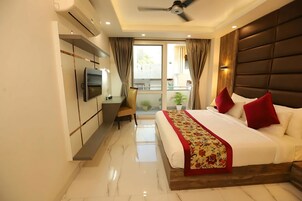 Quarto de hotel moderno com uma cama grande, uma escrivaninha, uma televisão e uma varanda com plantas.