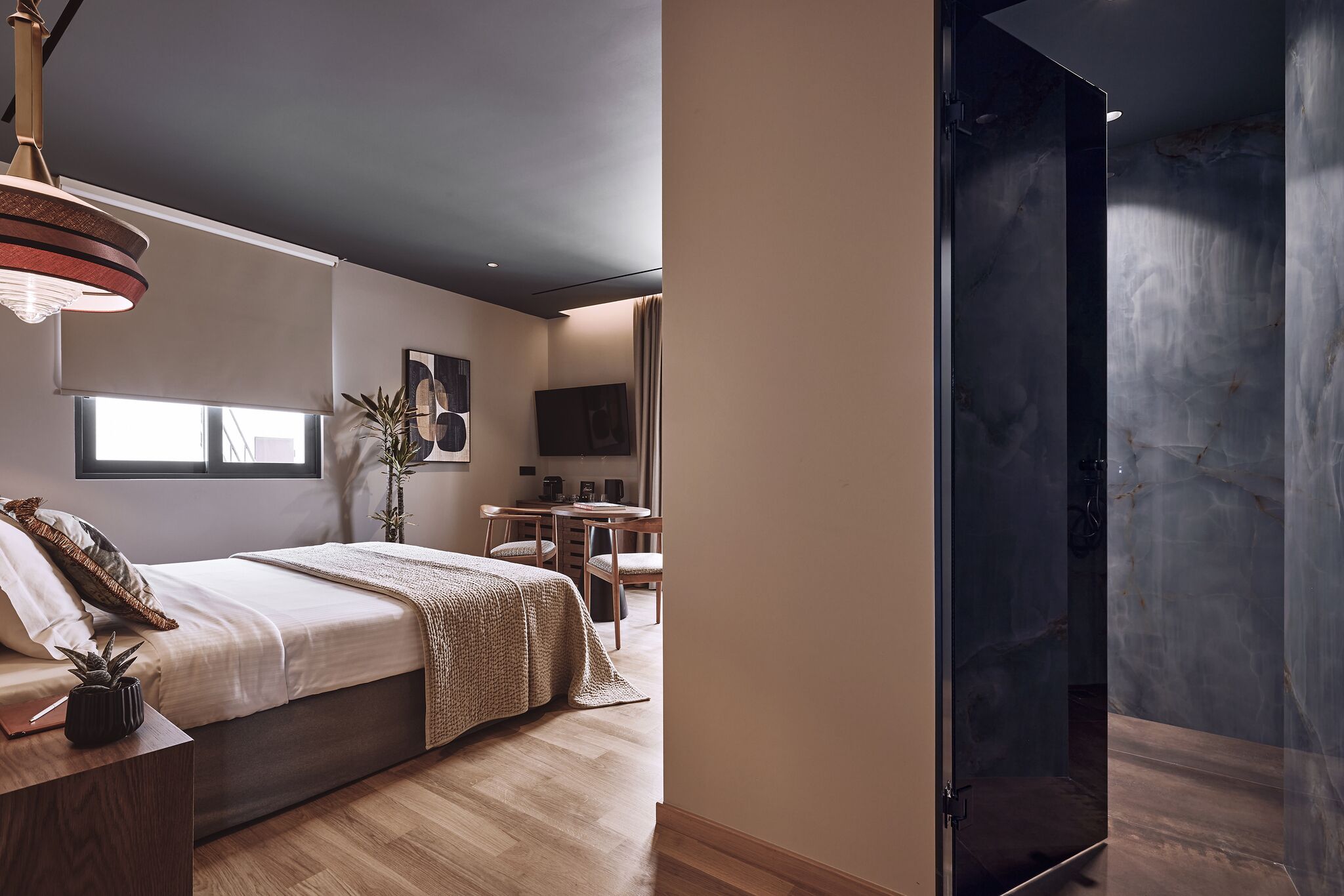 Um quarto moderno com uma cama, mesa de cabeceira e uma escrivaninha com cadeira. Há uma janela com persianas, uma planta e um quadro na parede.