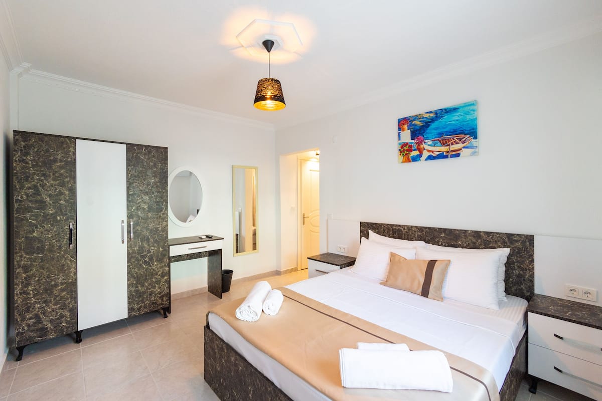 Quarto de hotel moderno com uma cama grande, um guarda-roupa, uma secretária com um espelho e um quadro na parede.