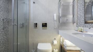 Uma casa de banho moderna com cabine de duche em vidro, sanita, lavatório com espelho e um porta-toalhas.