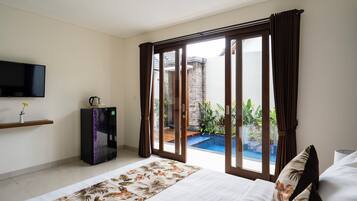 Quarto de hotel com cama, televisão de tela plana, minibar e vista para uma piscina.