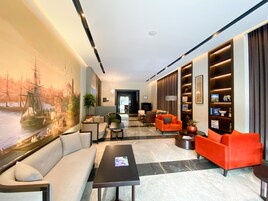 Um hall de hotel moderno com um grande mural, assentos confortáveis, uma mesa de recepção e interior bem iluminado.