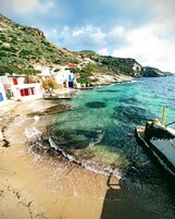 Uma área costeira com águas turquesa cristalinas, uma praia de areia e edifícios com fachadas vermelhas e brancas.