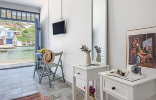 Quarto moderno com uma grande janela com vista para um corpo de água, uma cadeira com chapéu, uma escrivaninha com espelho e um quadro na parede.