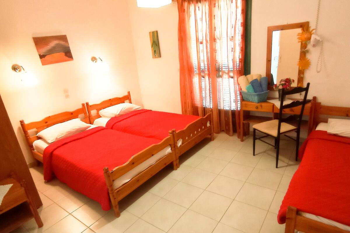 Quarto com duas camas de madeira, uma escrivaninha com cadeira, um espelho e uma janela com cortinas.