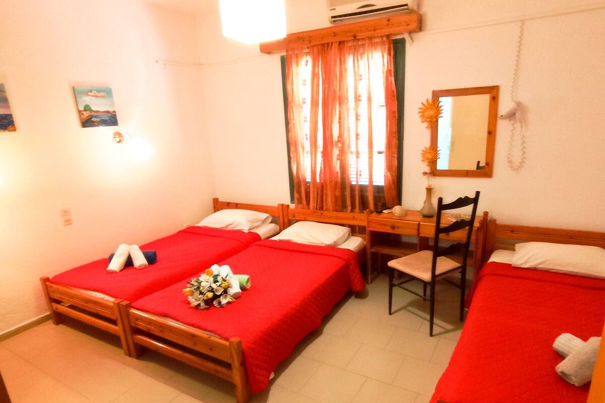 Quarto de hotel com duas camas de solteiro, uma escrivaninha de madeira, uma cadeira e uma mesa pequena.