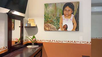 Quarto com televisão na parede, pintura de uma criança, pequena estante com uma placa e um detalhe decorativo na parede.