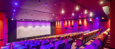Um cinema com fileiras de assentos, uma tela grande e um esquema de cores vermelho e roxo.