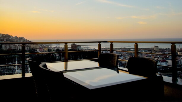 Varanda com mesa e cadeiras com vista para uma paisagem urbana ao pôr do sol.