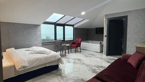 Quarto de hotel moderno com uma cama grande, um sofá vermelho, uma área de estar com cadeiras, uma banheira e um claraboia.