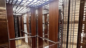 Interior de elevador com piso refletivo, portas de madeira e guarda-corrimão de metal.