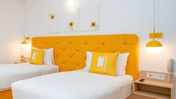 Quarto de hotel com duas camas, cabeceira amarela vibrante, roupa de cama branca e telefone fixado na parede.