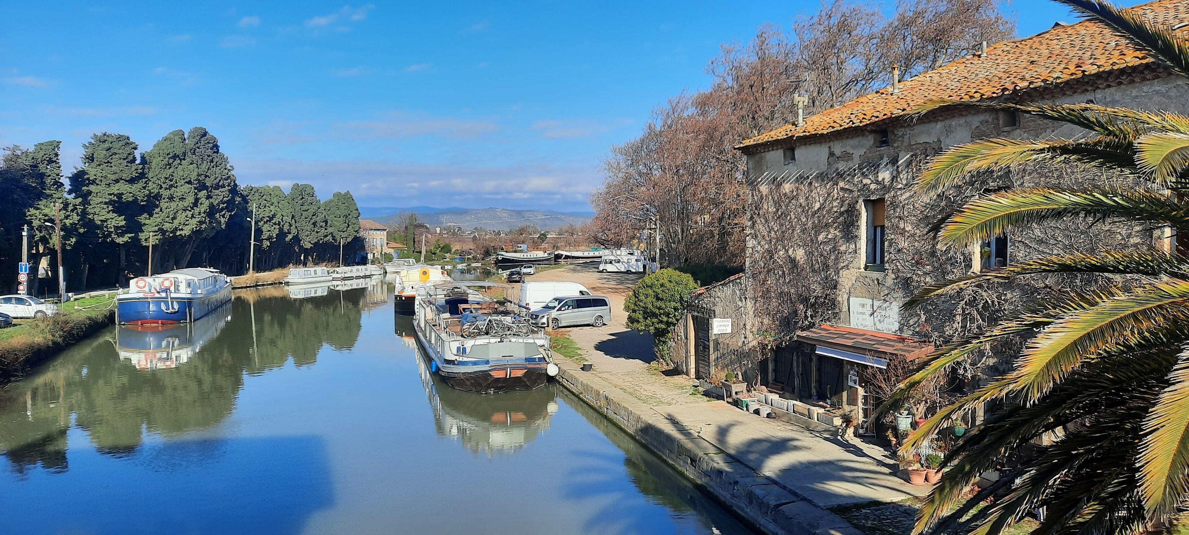 Um canal com barcos, um edifício com telhado de azulejos e árvores ao longo da margem.