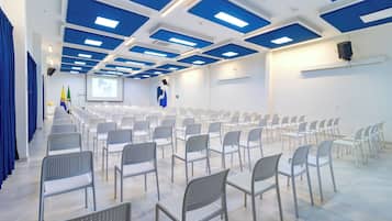 Sala de conferências com fileiras de cadeiras, uma tela de projetor e um design de teto azul e branco.