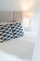 Cama com roupa de cama branca e almofada estampada em azul e branco.