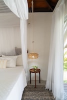 Quarto com cama de dossel, luminária pendente e uma pequena mesa com uma planta.