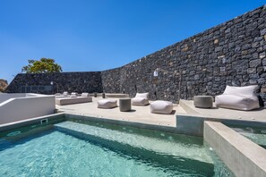Área de piscina com paredes de pedra, cadeiras de descanso e uma piscina azul cristalina.