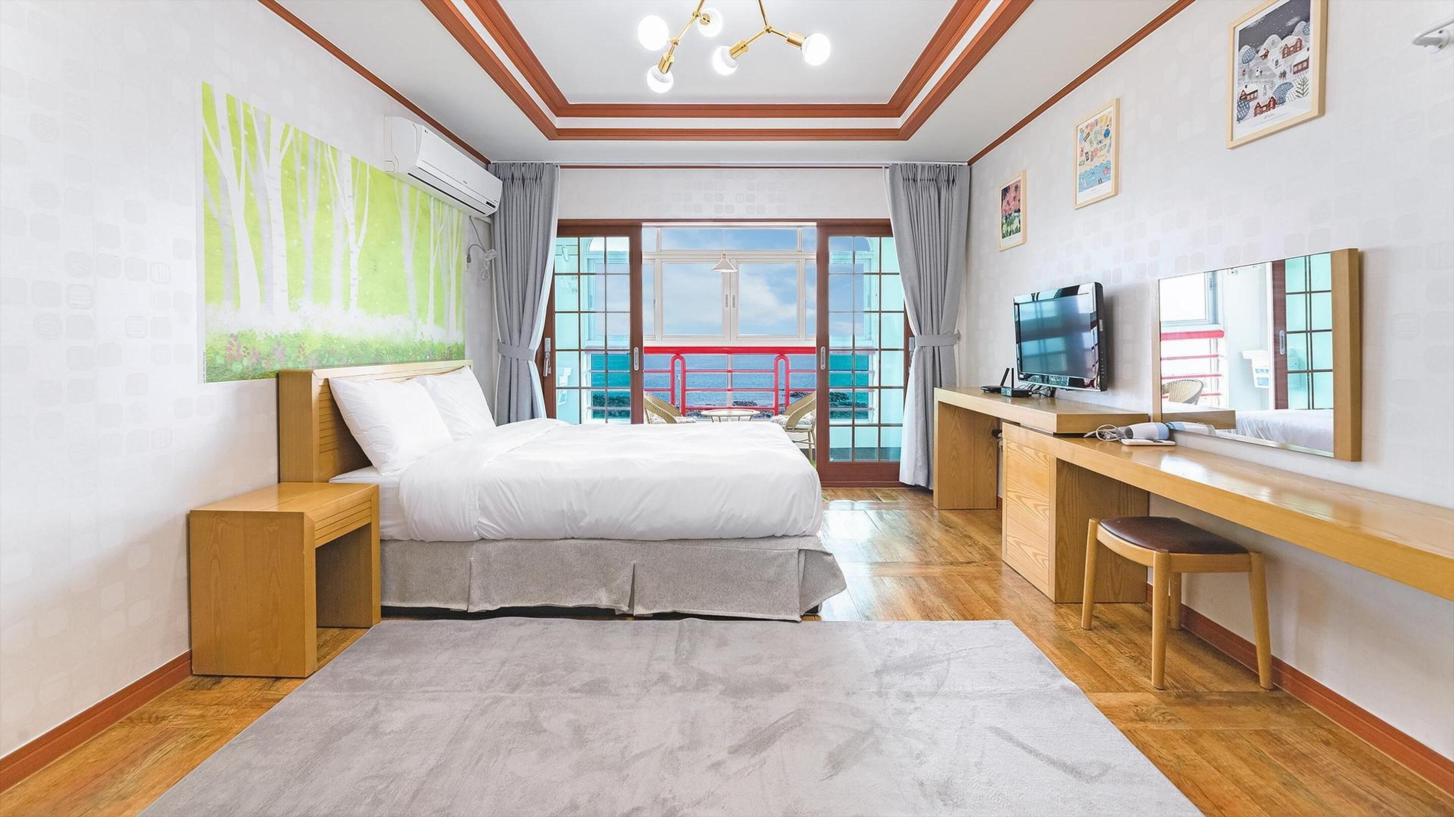Quarto de hotel com cama, escrivaninha com televisão, janela ampla com vista e um quadro na parede.