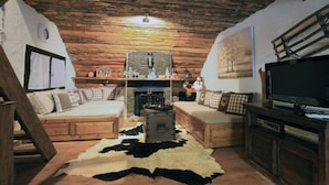 Interior acolhedor de uma cabana de madeira com lareira, móveis de madeira e uma televisão.