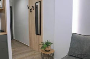 Um corredor com parede de painéis de madeira, um espelho, uma pequena mesa redonda com uma planta e um sofá cinzento.
