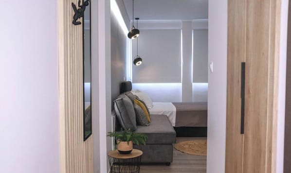Um quarto moderno e minimalista com um sofá cinzento, uma mesinha redonda com uma planta e um candeeiro suspenso.