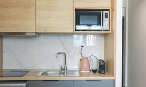 Uma cozinha com micro-ondas, chaleira e cafeteira sobre a bancada.