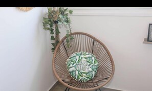 Uma cadeira de vime com almofada estampada com tema tropical e o texto 'ENJOY every moment of PARADISE'.