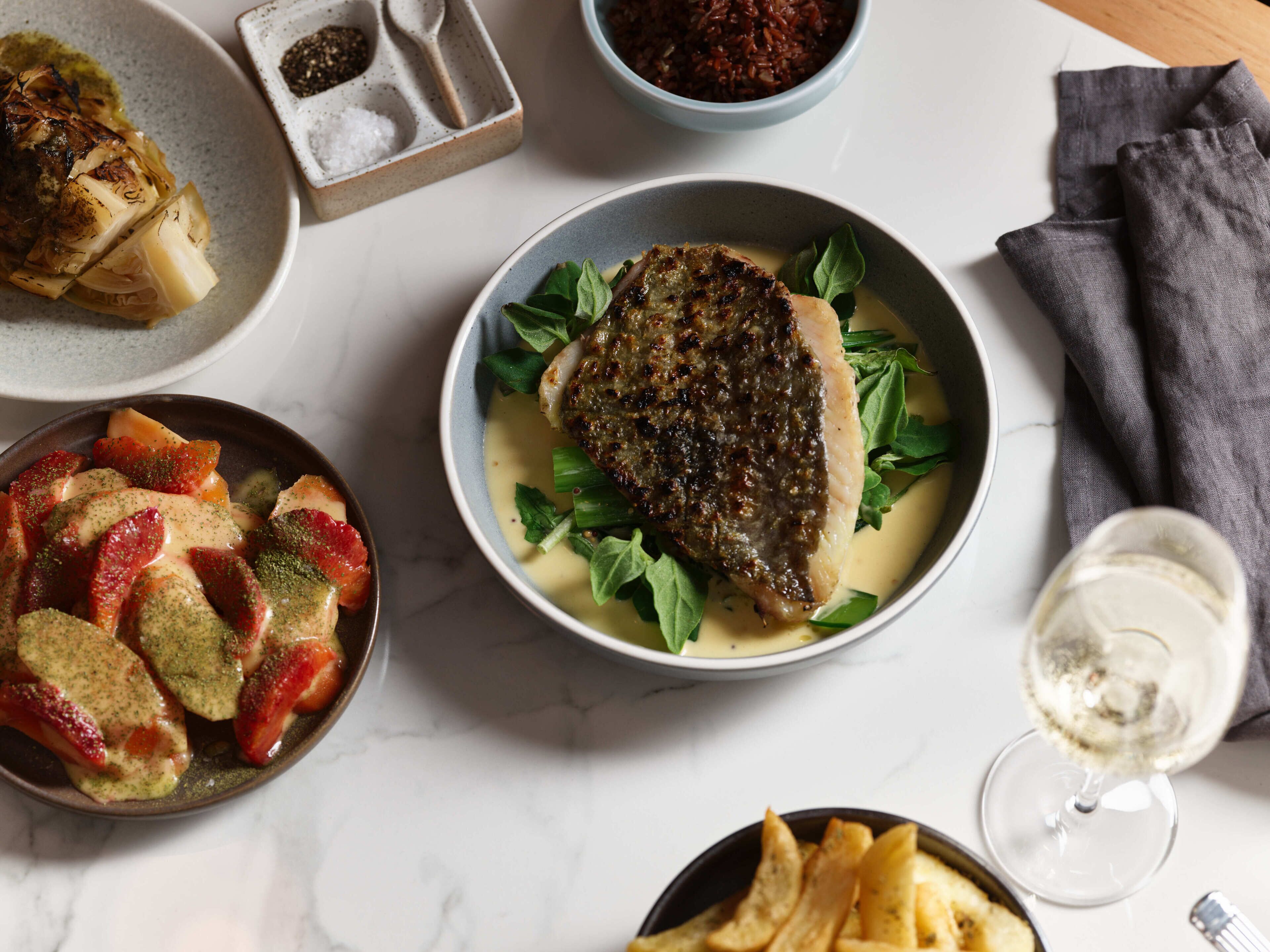 Uma mesa de jantar com diversos pratos, incluindo bife, legumes e uma taça de vinho.