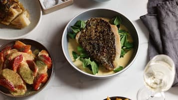 Uma mesa de jantar com diversos pratos, incluindo bife, legumes e uma taça de vinho.