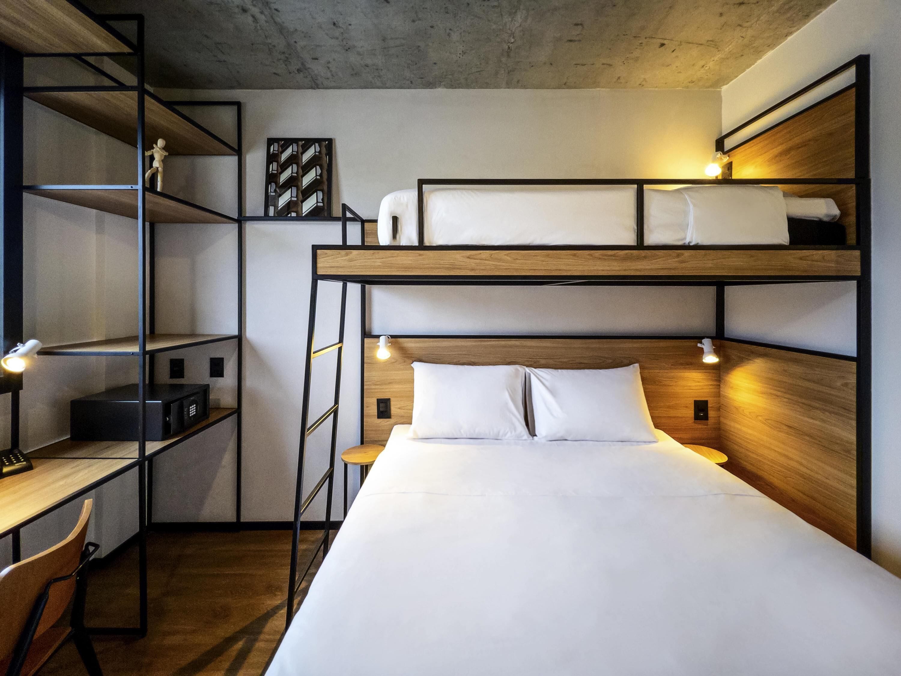 Quarto com beliche, escrivaninha e prateleiras, uma escada e uma pequena mesa com abajur.