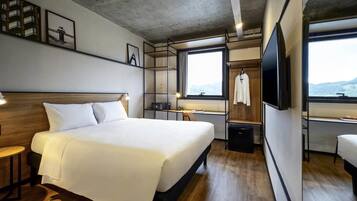 Quarto de hotel moderno com uma cama grande, mesas de cabeceira, escrivaninha, televisão e janela com vista.