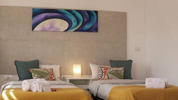 Quarto de hotel com duas camas, uma mesinha de cabeceira, um quadro na parede e um abajur.