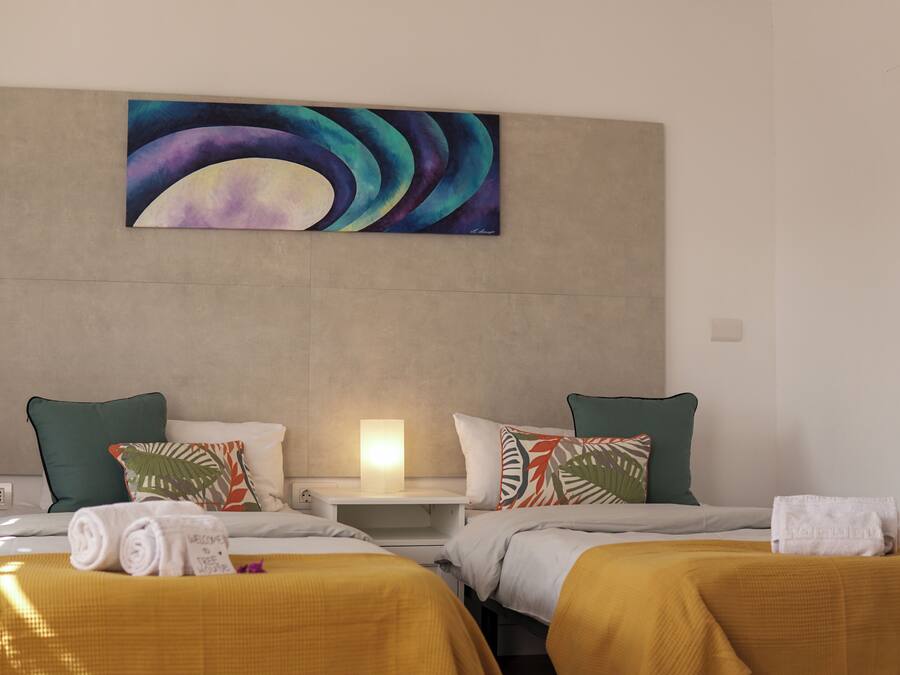 Quarto de hotel com duas camas, uma mesinha de cabeceira, um quadro na parede e um abajur.