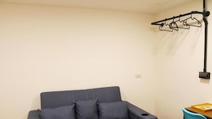 Um quarto com um sofá cinzento, uma cadeira azul e um cabideiro preto com ganchos.