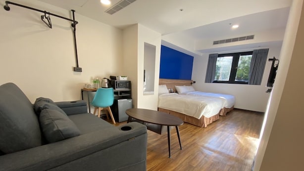 Quarto de hotel moderno com sofá, uma mesa pequena, cozinha compacta e cama com duas almofadas.