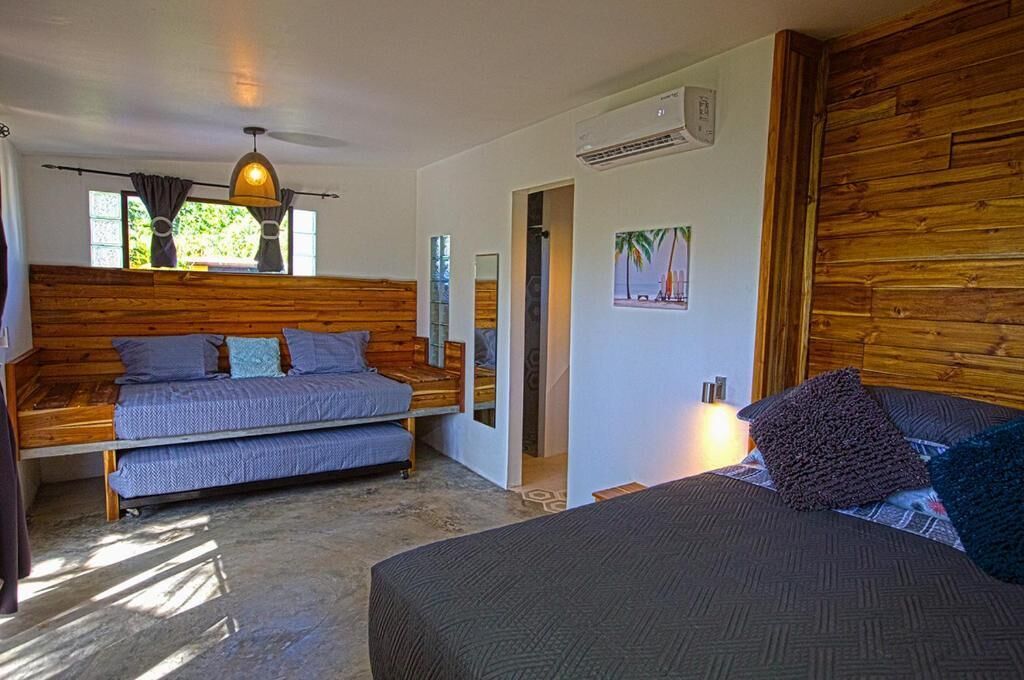 Quarto com cabeceira de cama em madeira, sofá-cama, ventoinha no teto e janela com cortinas.