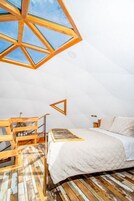 Um quarto aconchegante com estrutura de teto em madeira, uma cama, uma mesinha e uma cadeira.