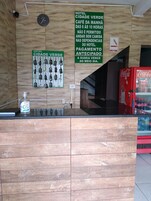 Bancada de recepção de hotel com um relógio, um aviso detalhando as comodidades do hotel e uma máquina de refrigerantes Coca-Cola.