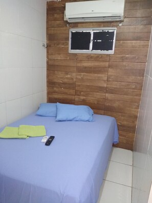 Uma cama de solteiro com colchão e almofadas azuis, um controle remoto e uma toalha verde sobre a cama.