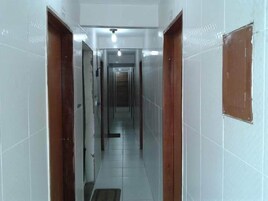 Um corredor estreito, com piso de azulejos e portas de madeira em ambos os lados, que dá acesso a vários quartos.