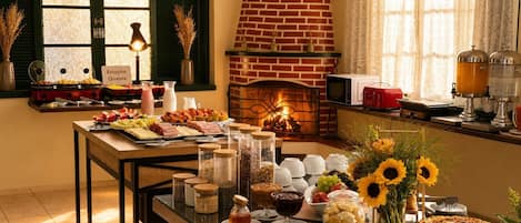 Um buffet de café da manhã com diversos alimentos e uma lareira de tijolos ao fundo.