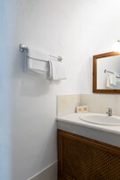 Casa de banho com uma sanita branca, toucador de madeira, porta-toalhas com duas toalhas brancas e um espelho com moldura de madeira.