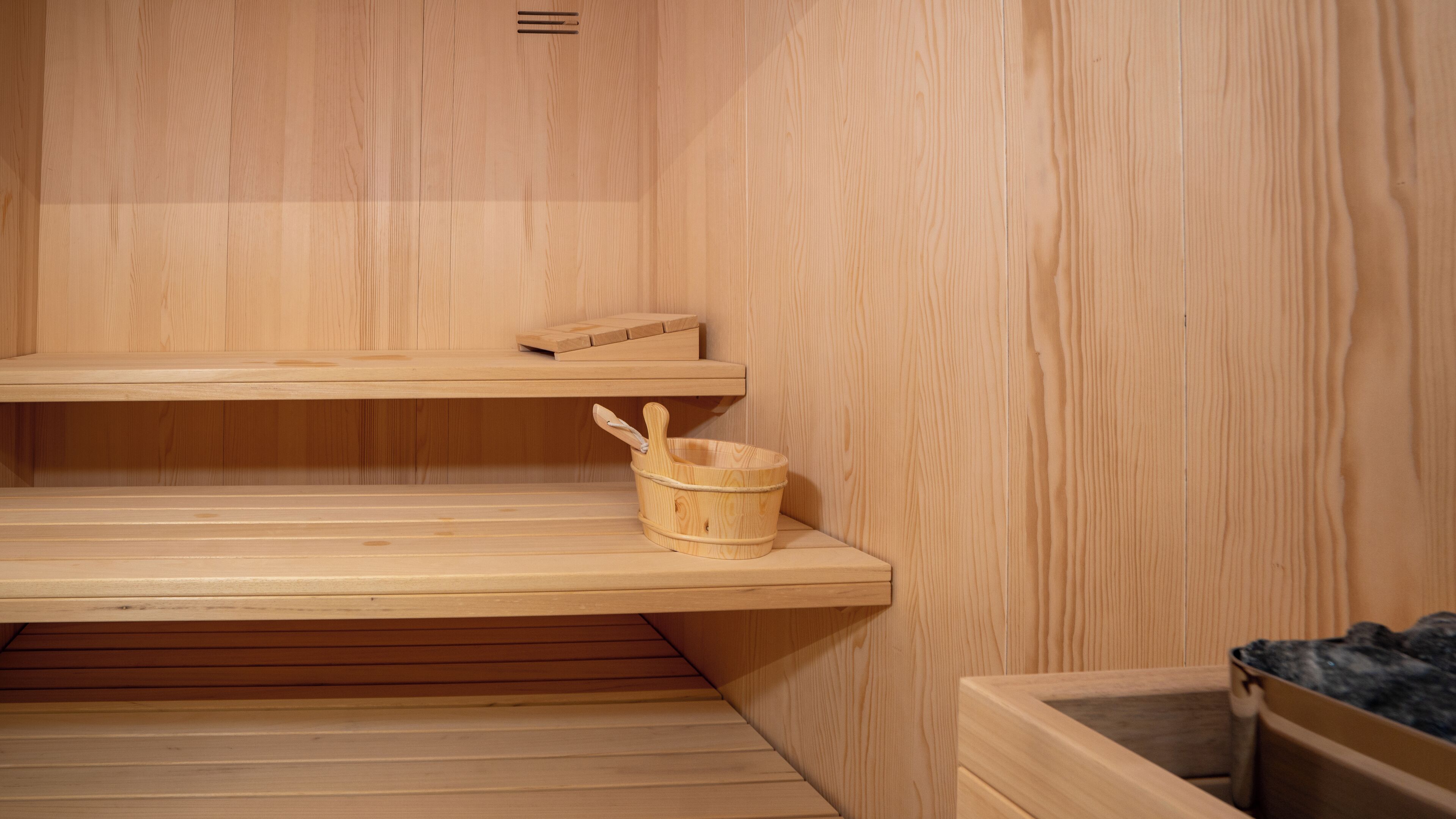 Uma sauna de madeira com um banco, um balde e uma caixa, todos em madeira.