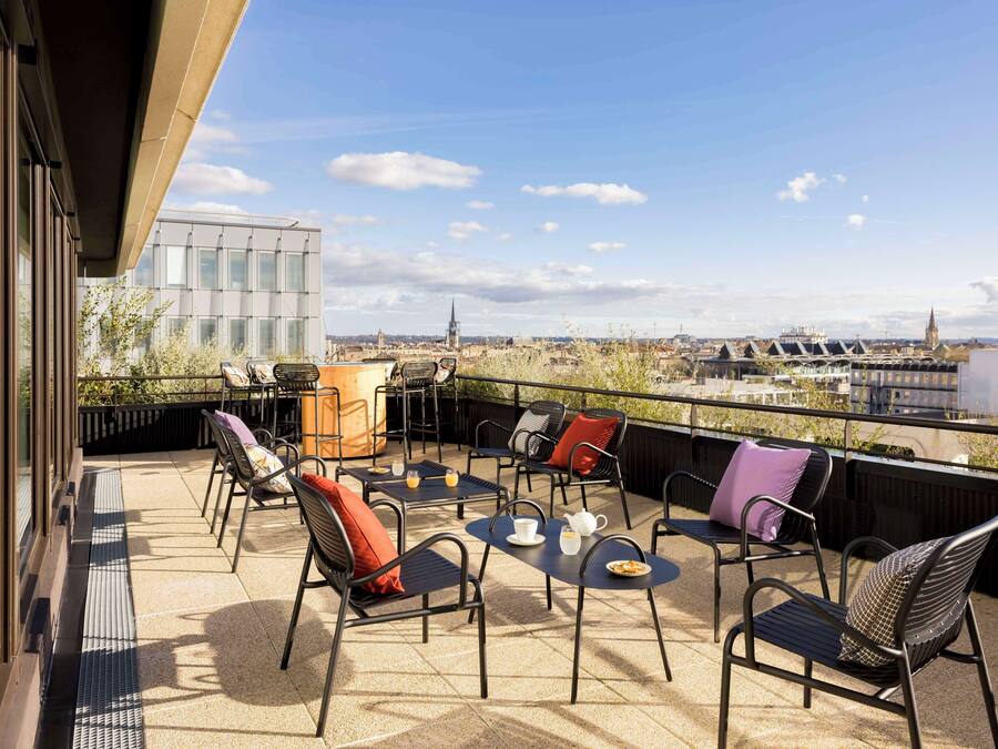 Terraço no telhado com área de estar externa, uma mesa com bule e vista para a paisagem urbana.