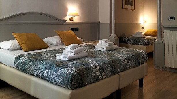 Quarto de hotel com uma cama grande, duas mesinhas de cabeceira, um criado-mudo, um espelho e um quadro na parede.