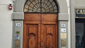Uma porta dupla de madeira com um arco decorativo acima, ladeada por placas e um detector de incêndio.
