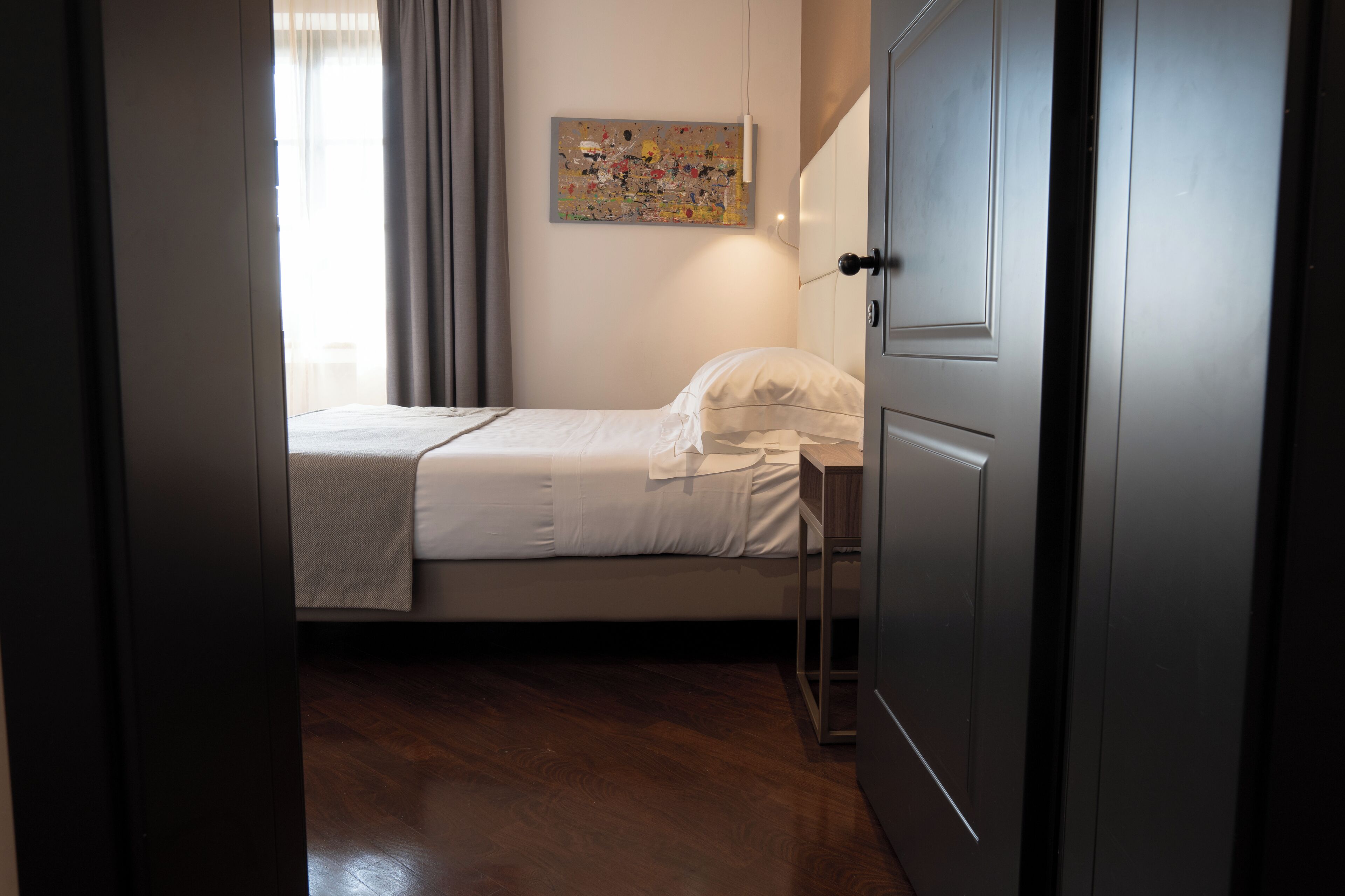 Quarto com cama, mesa de cabeceira, quadro na parede e porta.