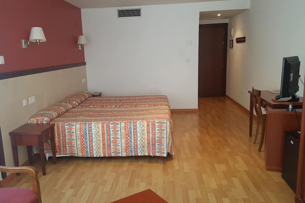 Quarto com cama de casal, uma escrivaninha com computador e uma cadeira.